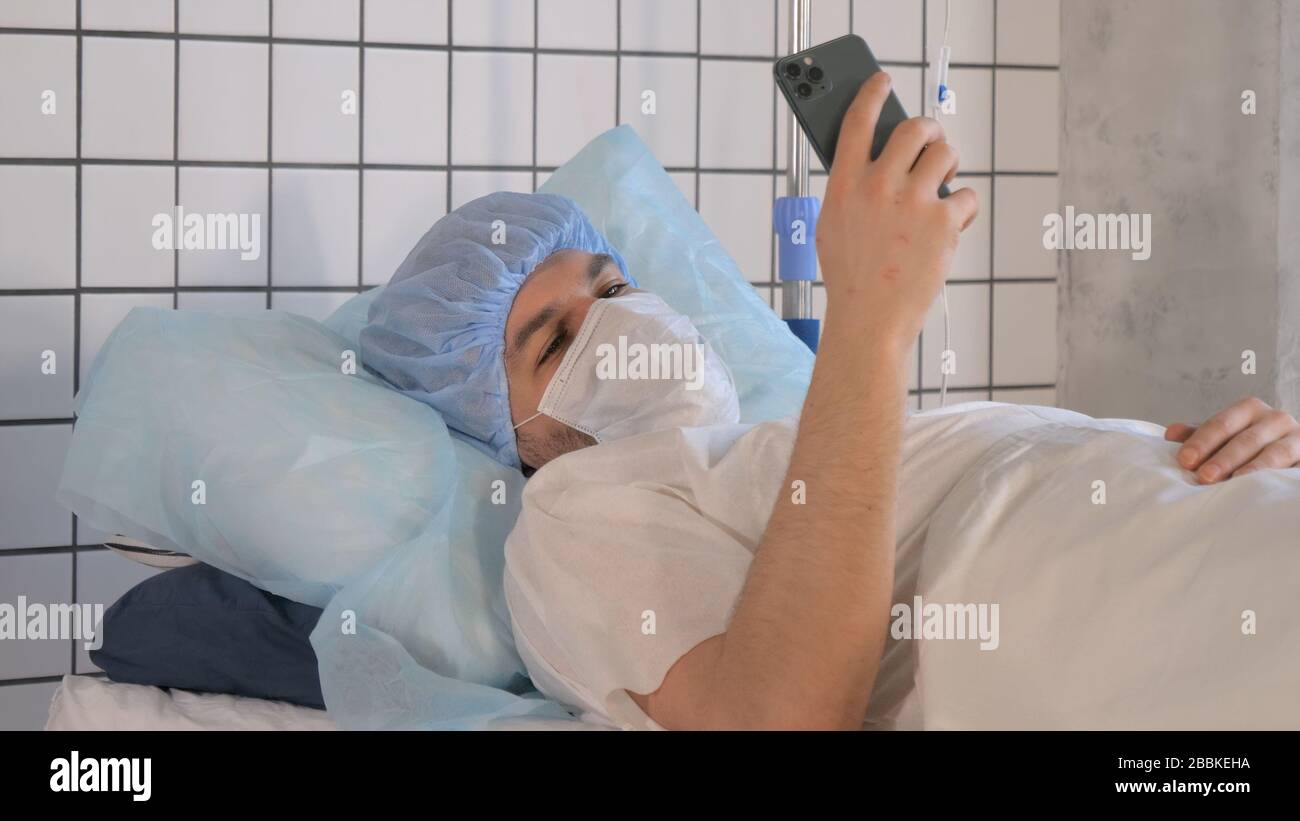 Male patient holding mobile phone while resting on bed in hospital ...