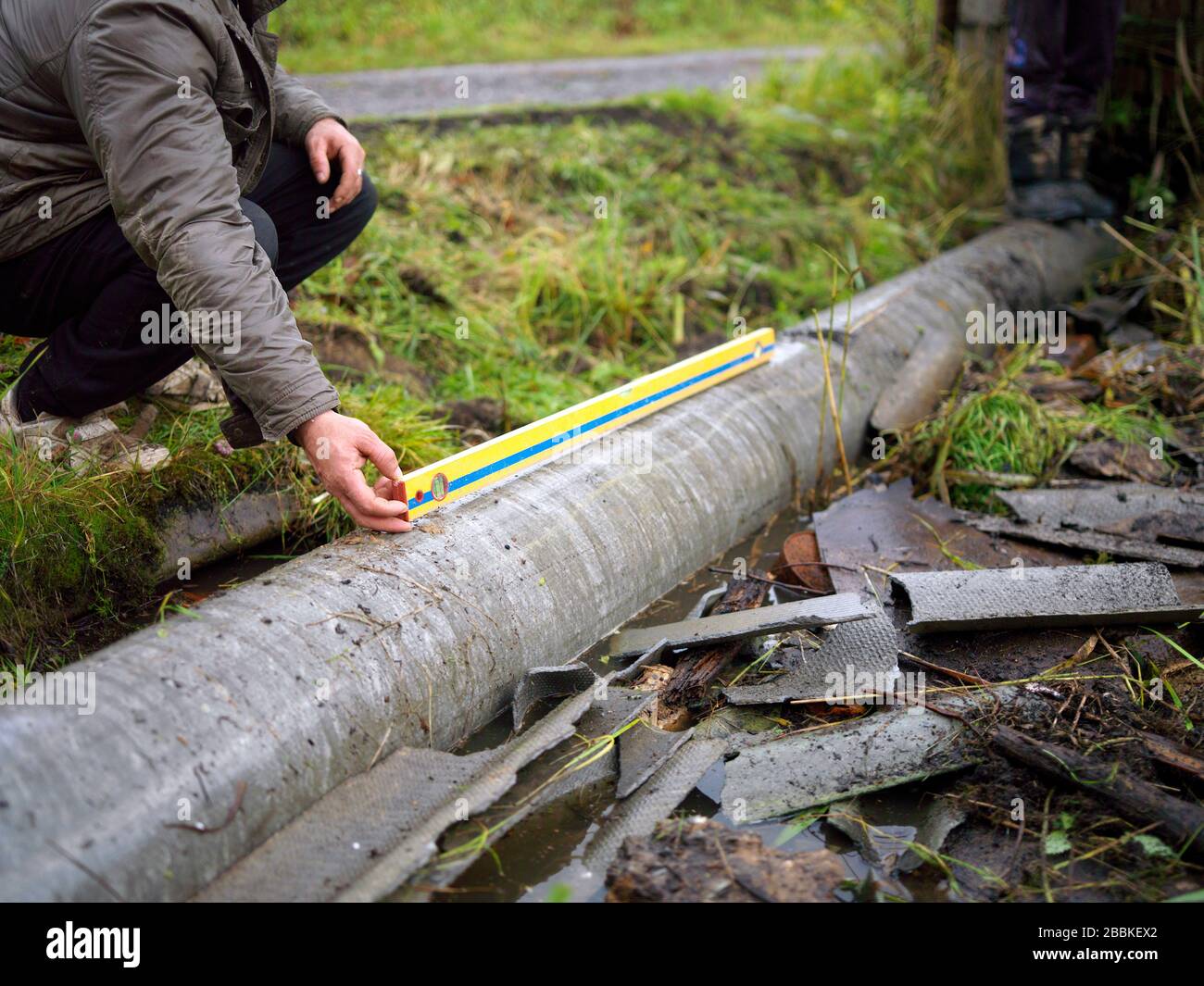 A pipe in a trench and a worker with a level ruler in hand, outdoor ...
