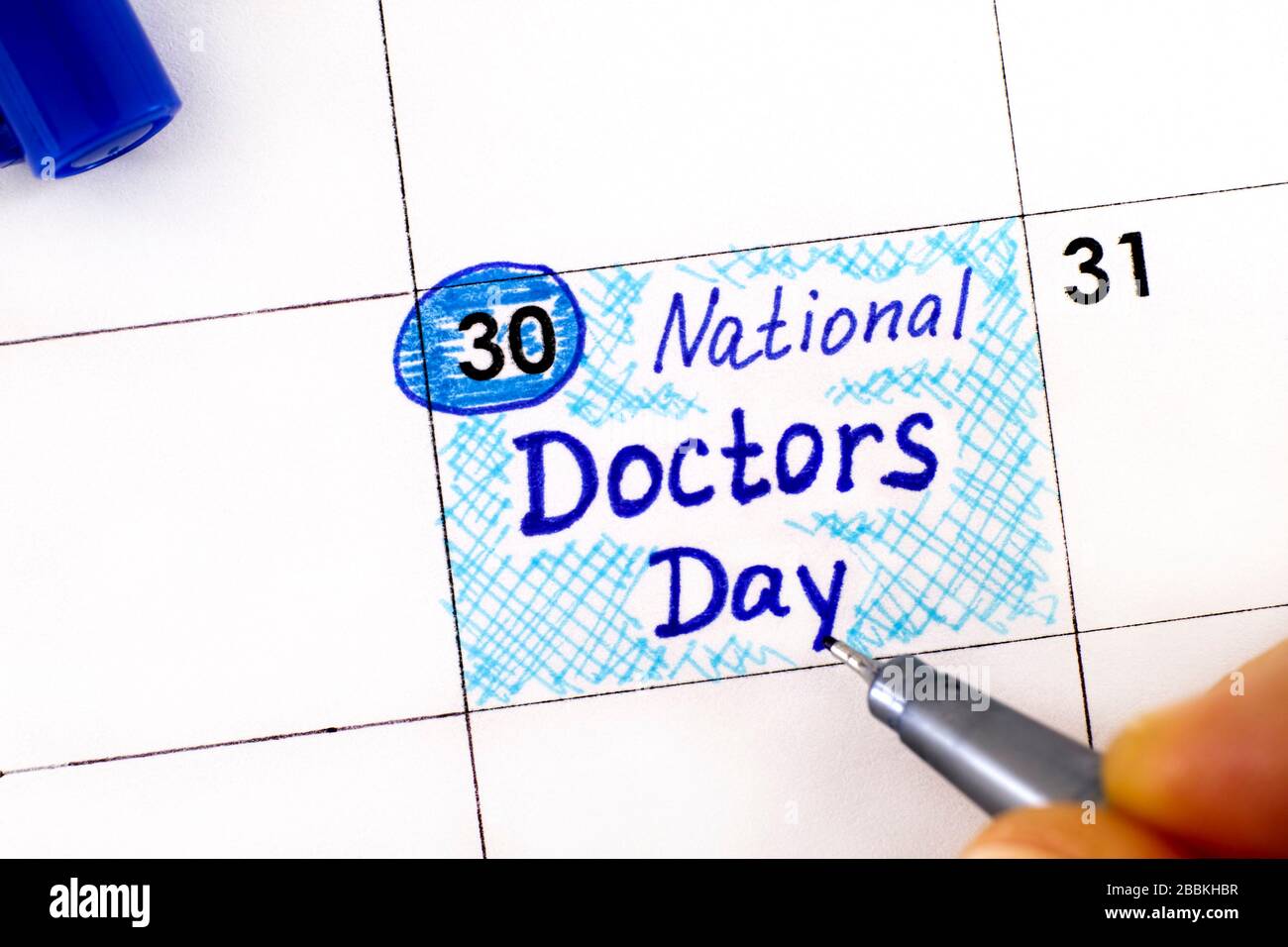 Woman fingers with pen writing reminder National Doctors Day in ...