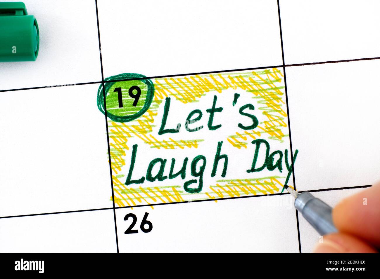 Woman fingers with pen writing reminder Let's Laugh Day in calendar ...