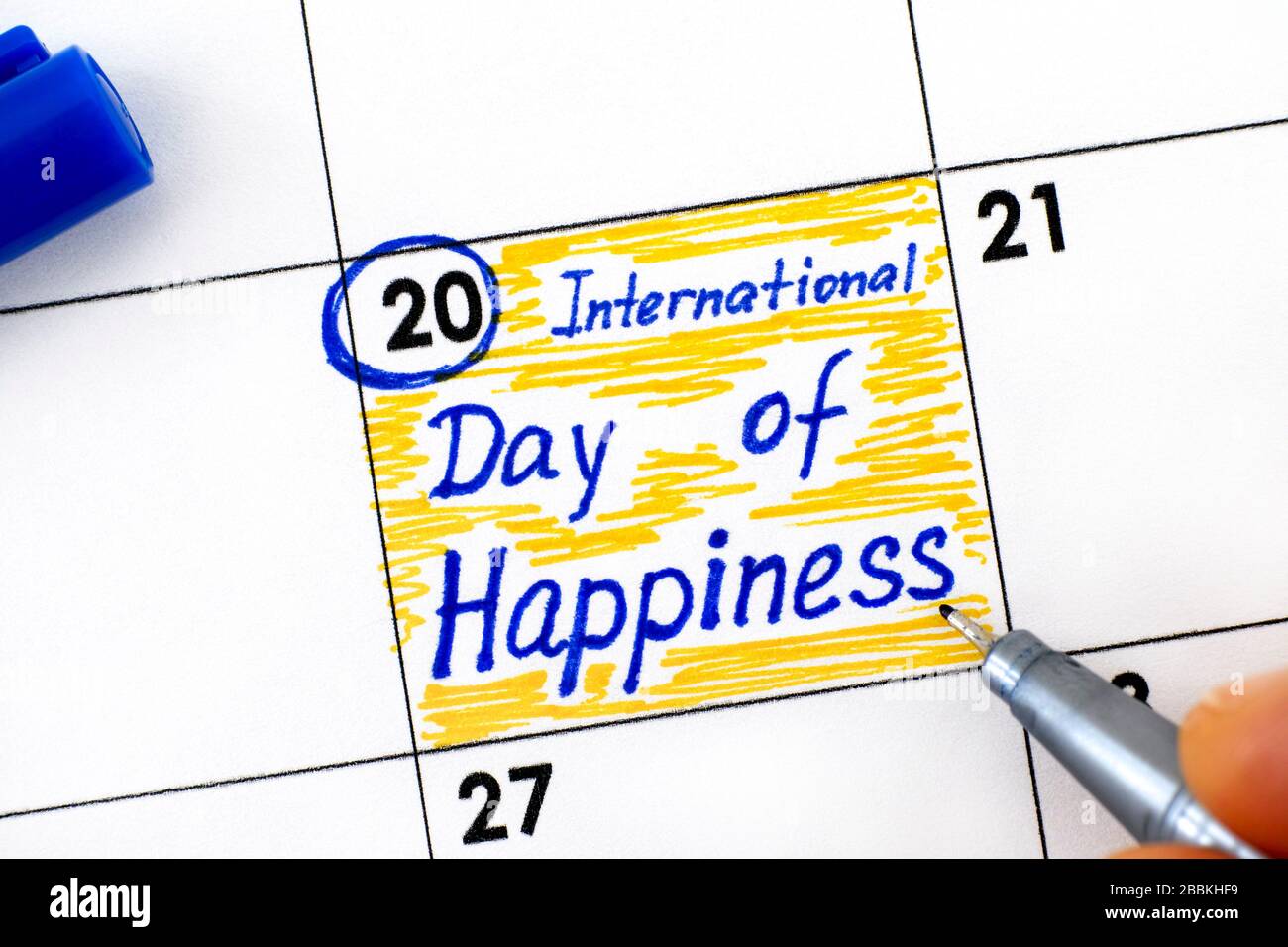 Woman fingers with pen writing reminder International Day of Happiness ...