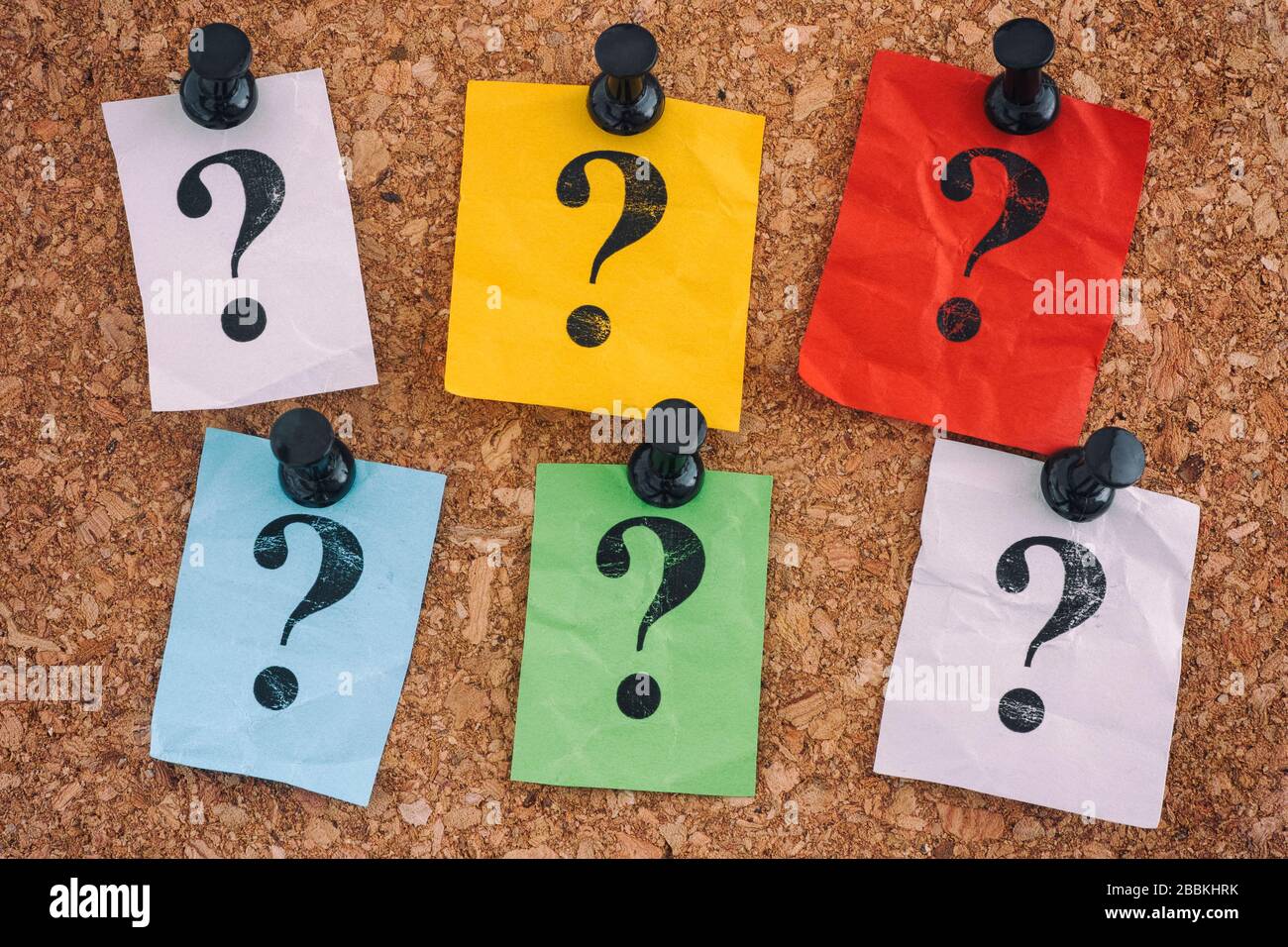 Colorful crumpled paper notes with question marks on a cork board ...
