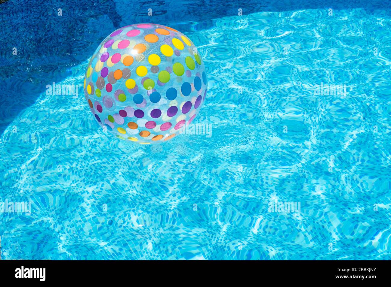 Inflatable colourful ball floating in blue swimming pool water at sunny ...