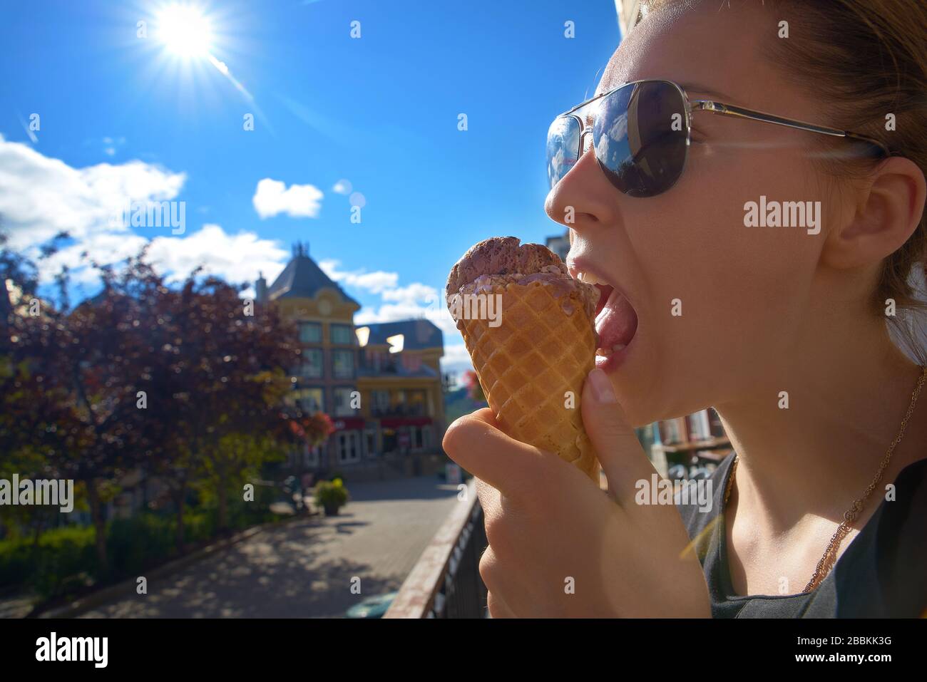 Pretty girl eats big ice-cream in hot weather in the city. Profile ...