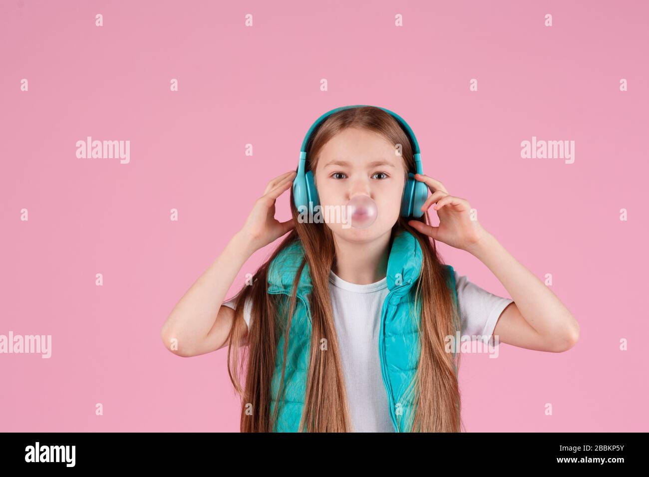 A little girl with headphones explodes pink chewing gum on a pink ...