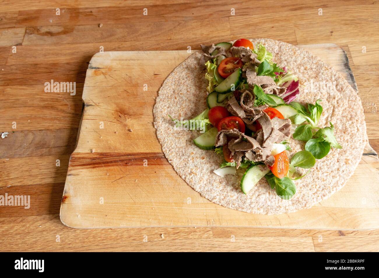 a close up view of a healthy ham and salad whole wheat wrap on a wooden ...