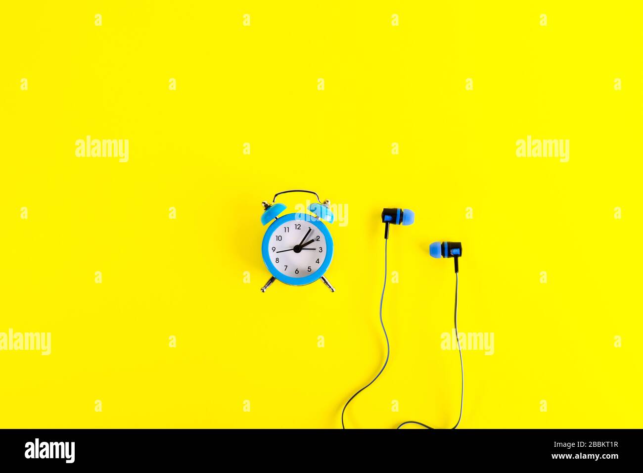 Small blue classic-style alarm clock and blue earphones in minimalist ...