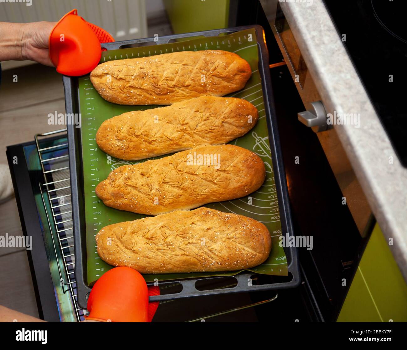Homemade bread on a baking sheet is taken out of the oven. Long loaf ...