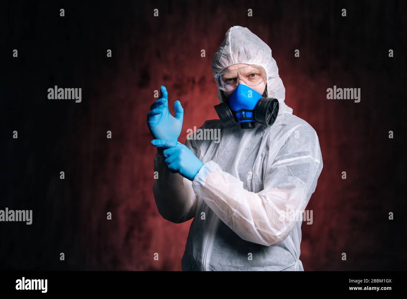 Scientist wearing hazmat, goggles and respirator slips on hands rubber ...