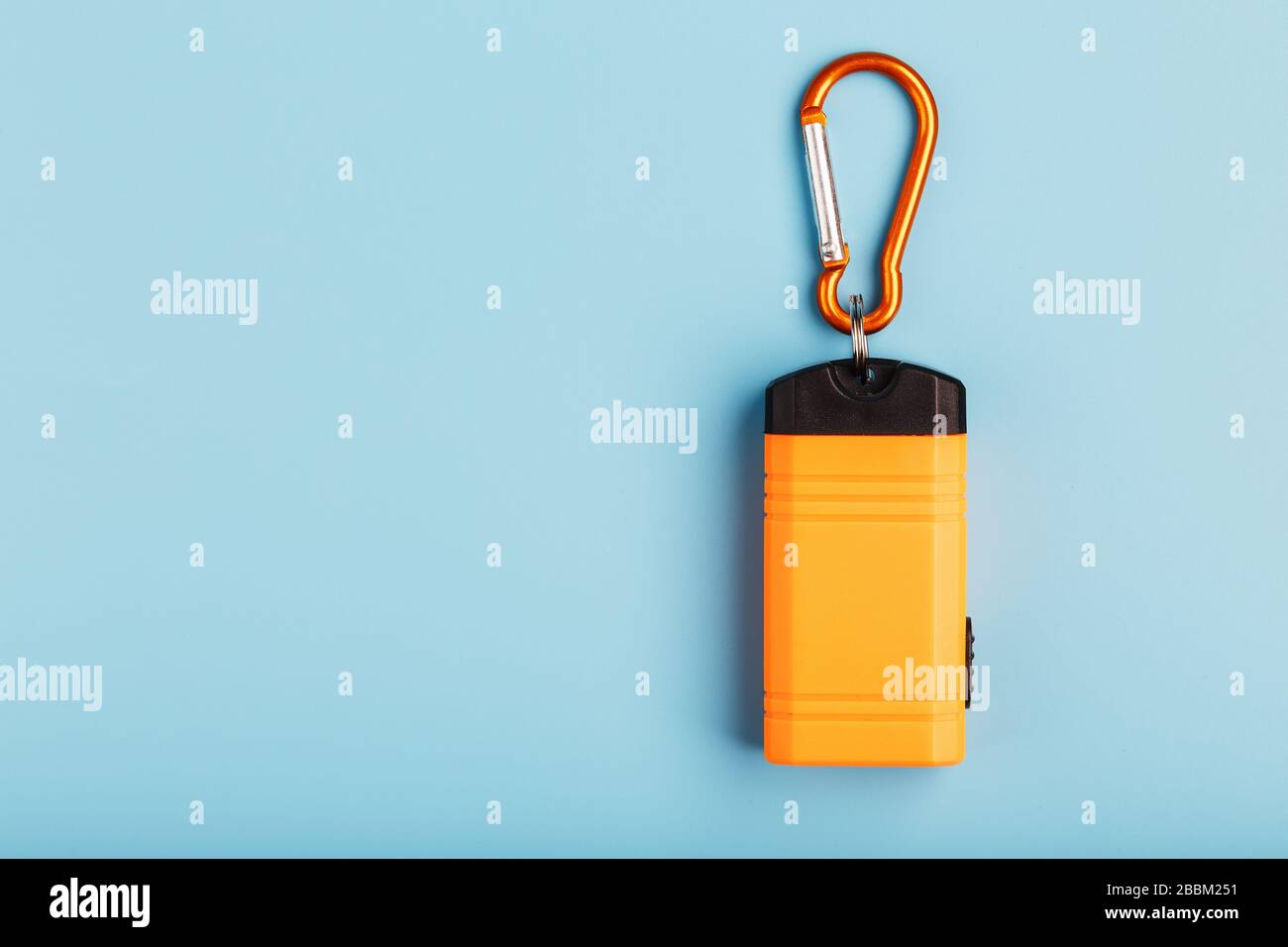 An orange led flashlight with a carabiner glows on a blue background ...