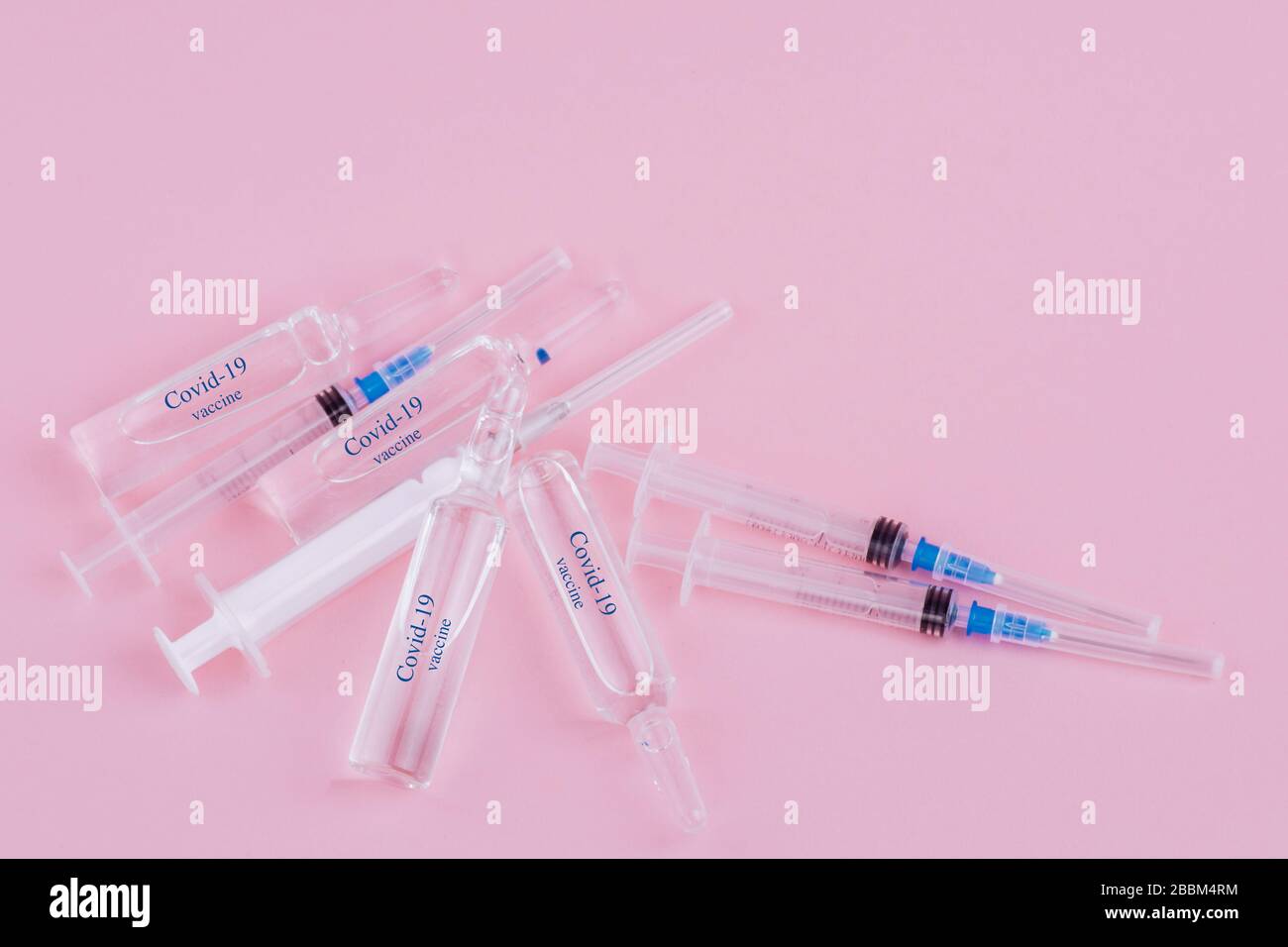 Plastic medical syringe with injection needles and ampoules on a pink ...