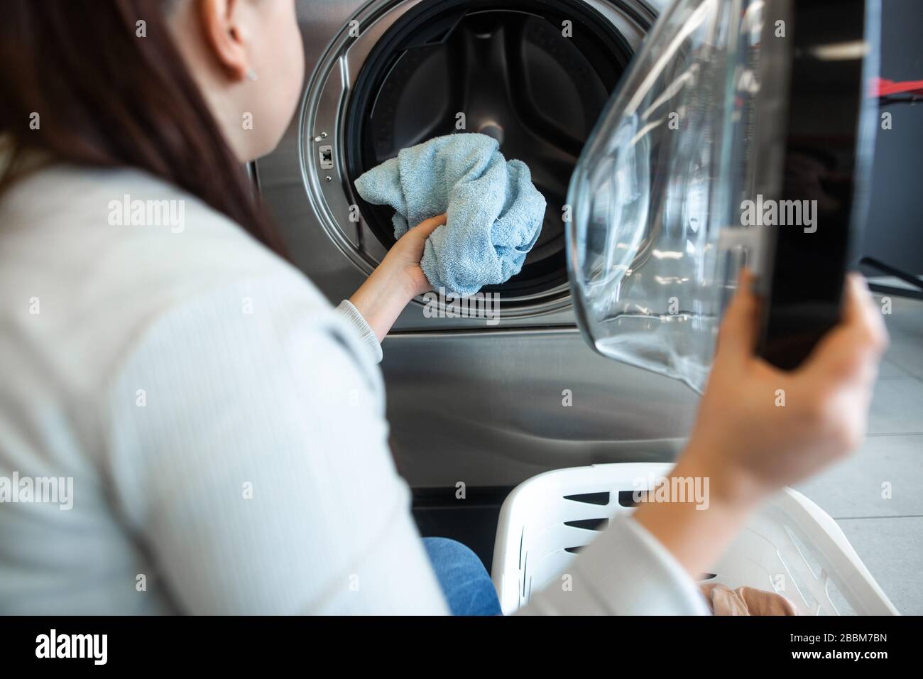 Pretty young woman putting, getting some dirty clothes into a washing ...