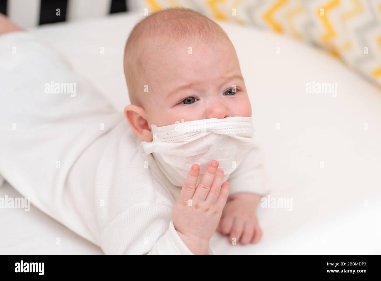 A newborn baby in a medical mask lies in quarantine at home during the ...