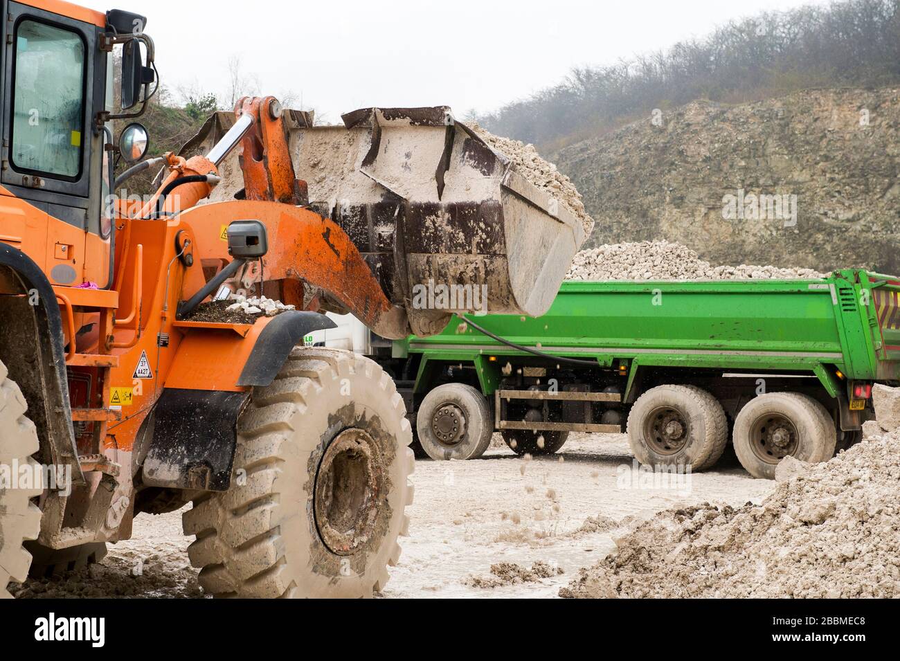 A digger with a load of aggregate tipping into a lorry at a quarry ...