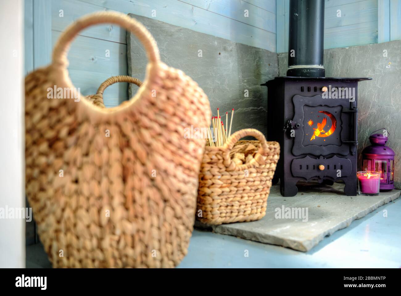 Glamping cosy log burner lit, with wicker baskets full of wood. England ...