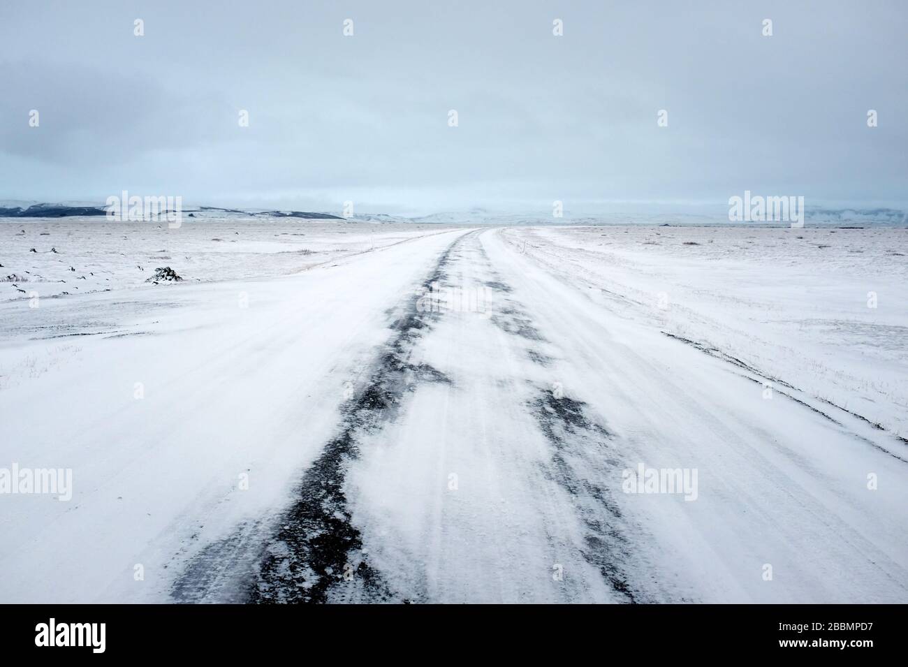 An empty frozen road in winter, covered in snow and ice leading off in ...