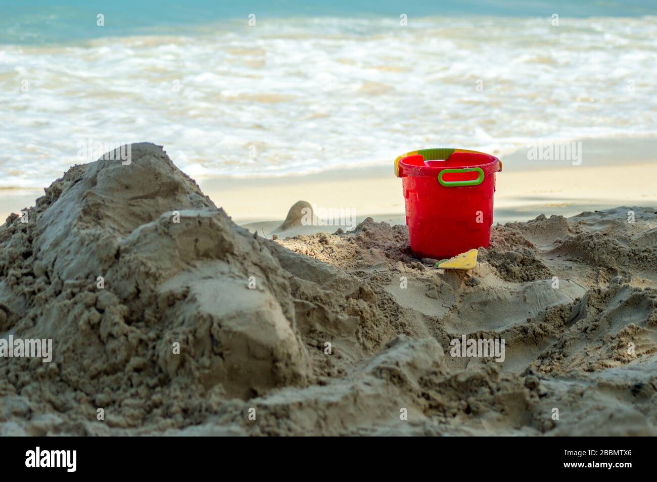 Bucket on a white sand beach next to a sandcastle in progress Stock ...