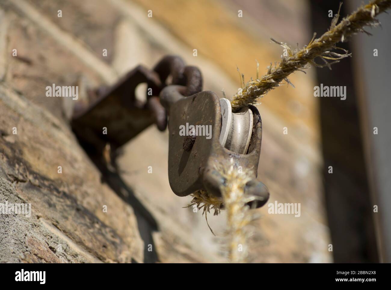 rusty pulley and hook fixed to a brick wall and holding a frayed ...