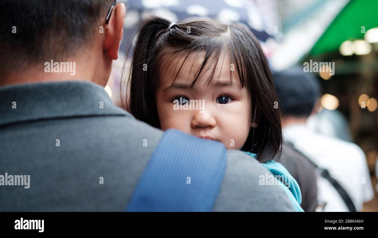 A sweet Japanese child, held by her father, looking back straight at ...