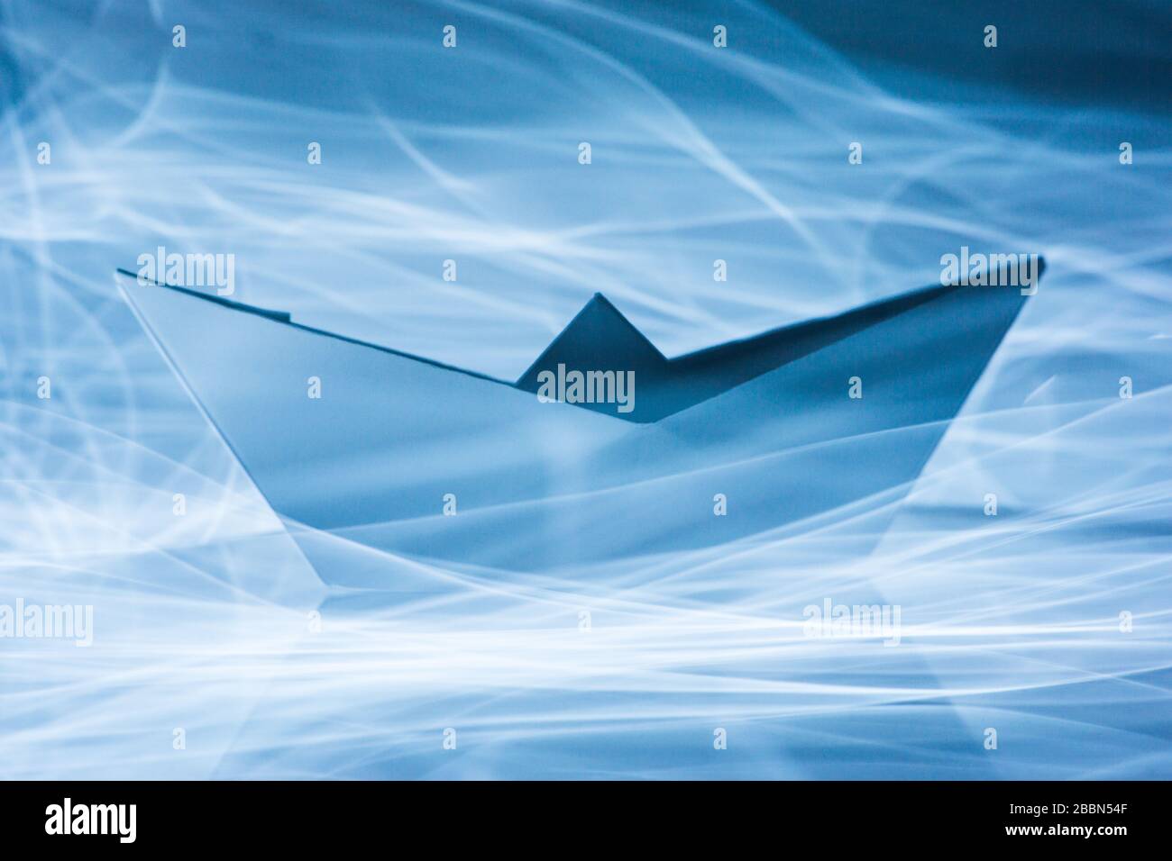 Paper boat splitting blue light trails symbolizing waves in the sea ...