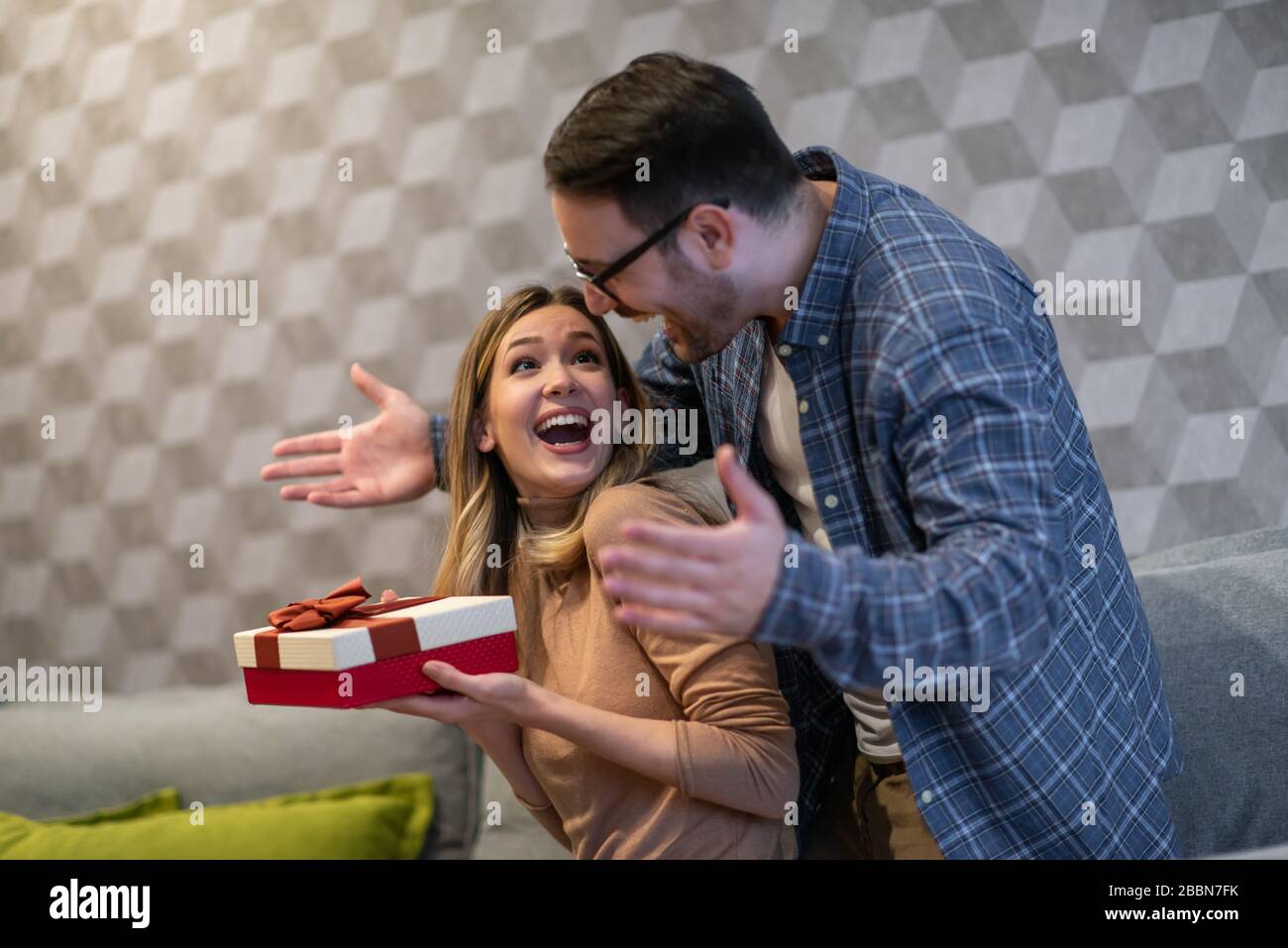Happy young couple celebrating at home.Man is giving his girlfriend a ...