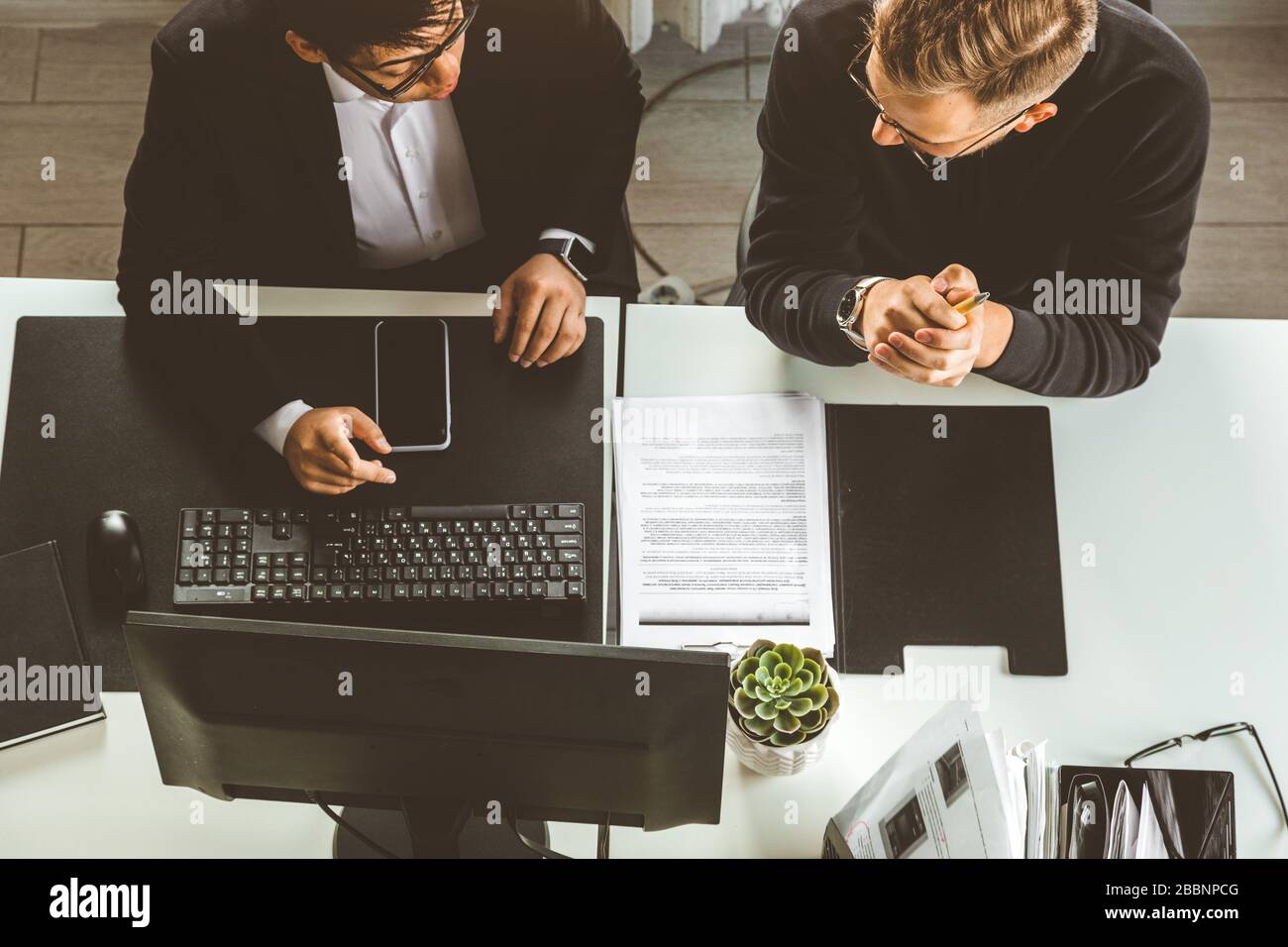 Young office worker sitting at desk, using computer. Two business man ...