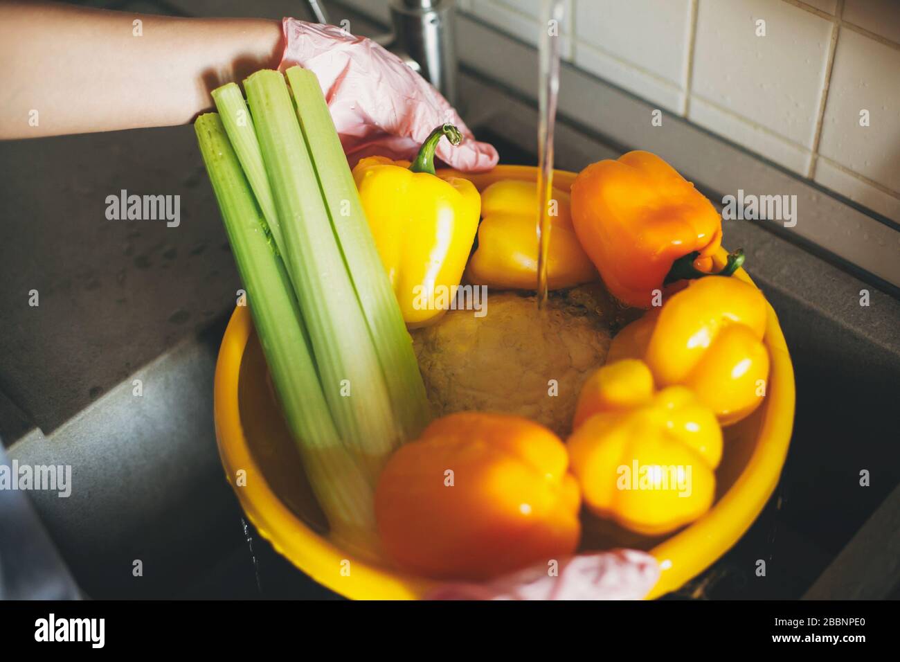 Washing vegetables. Hands in pink gloves washing vegetables in yellow ...