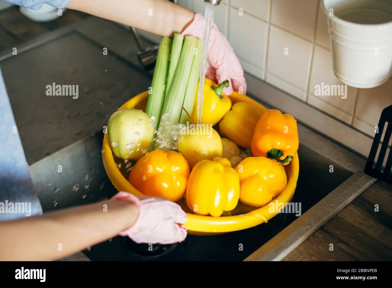 Washing vegetables. Hands in pink gloves washing vegetables in yellow ...
