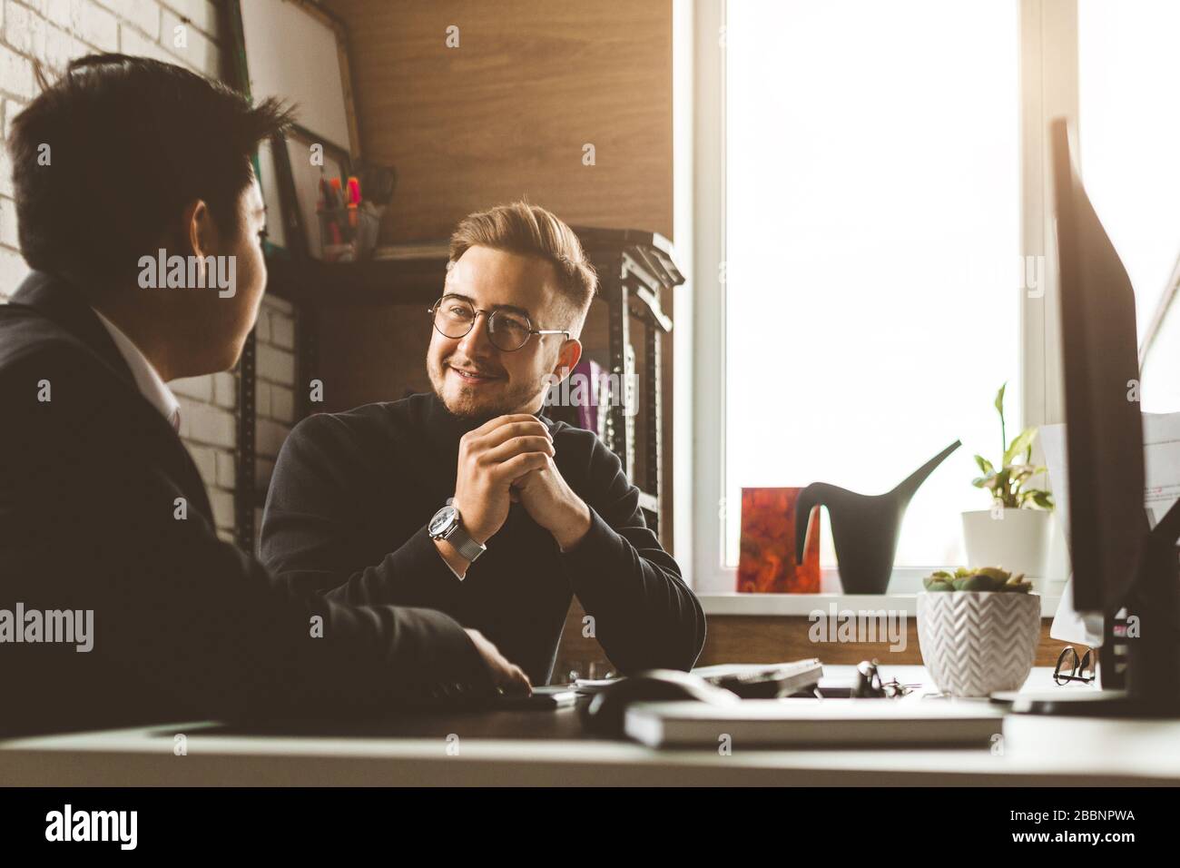 Young office worker sitting at desk, using computer. Two business man ...