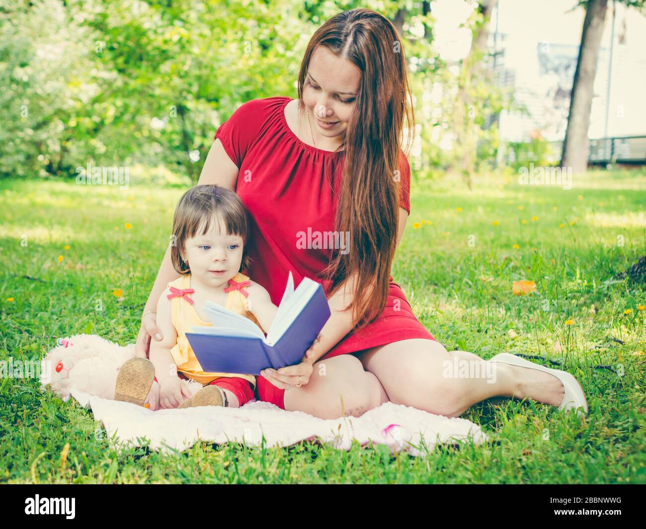 Mother and daughter reading book outdoors on grass at park Stock Photo ...