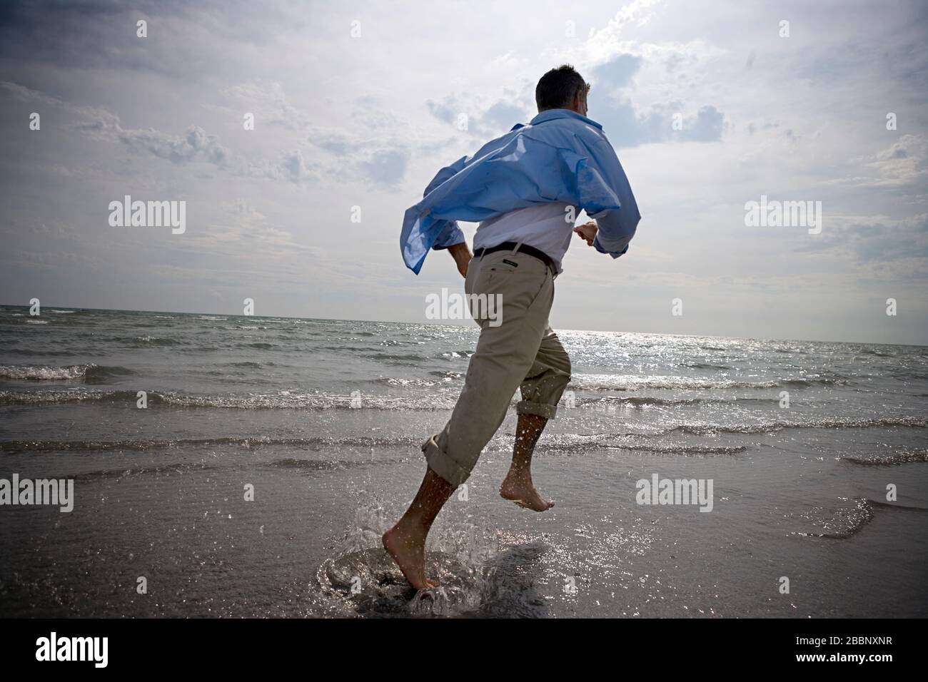 Mature man running through shallow water at the beach Stock Photo - Alamy