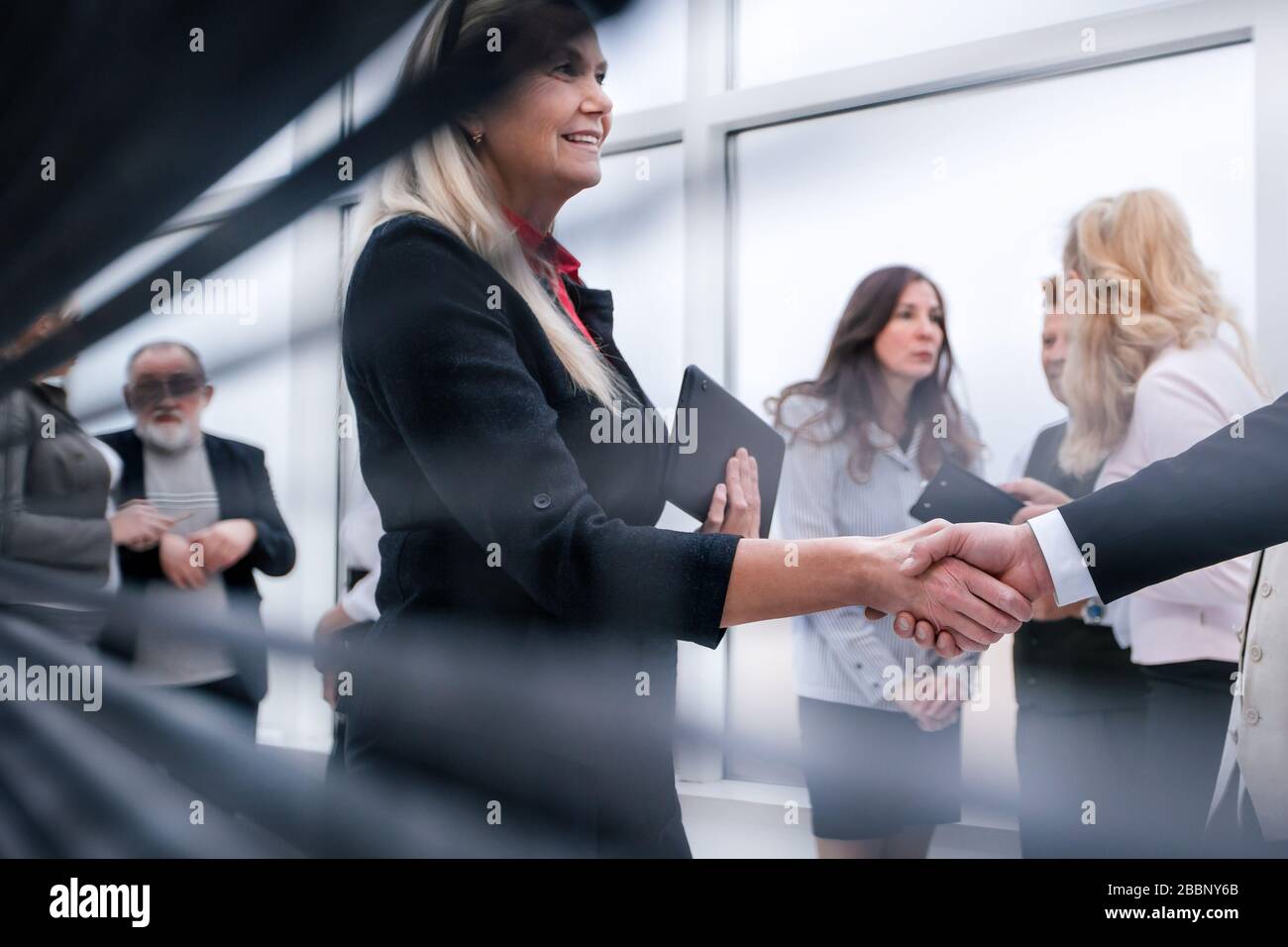 business people shaking hands while standing near an office window ...