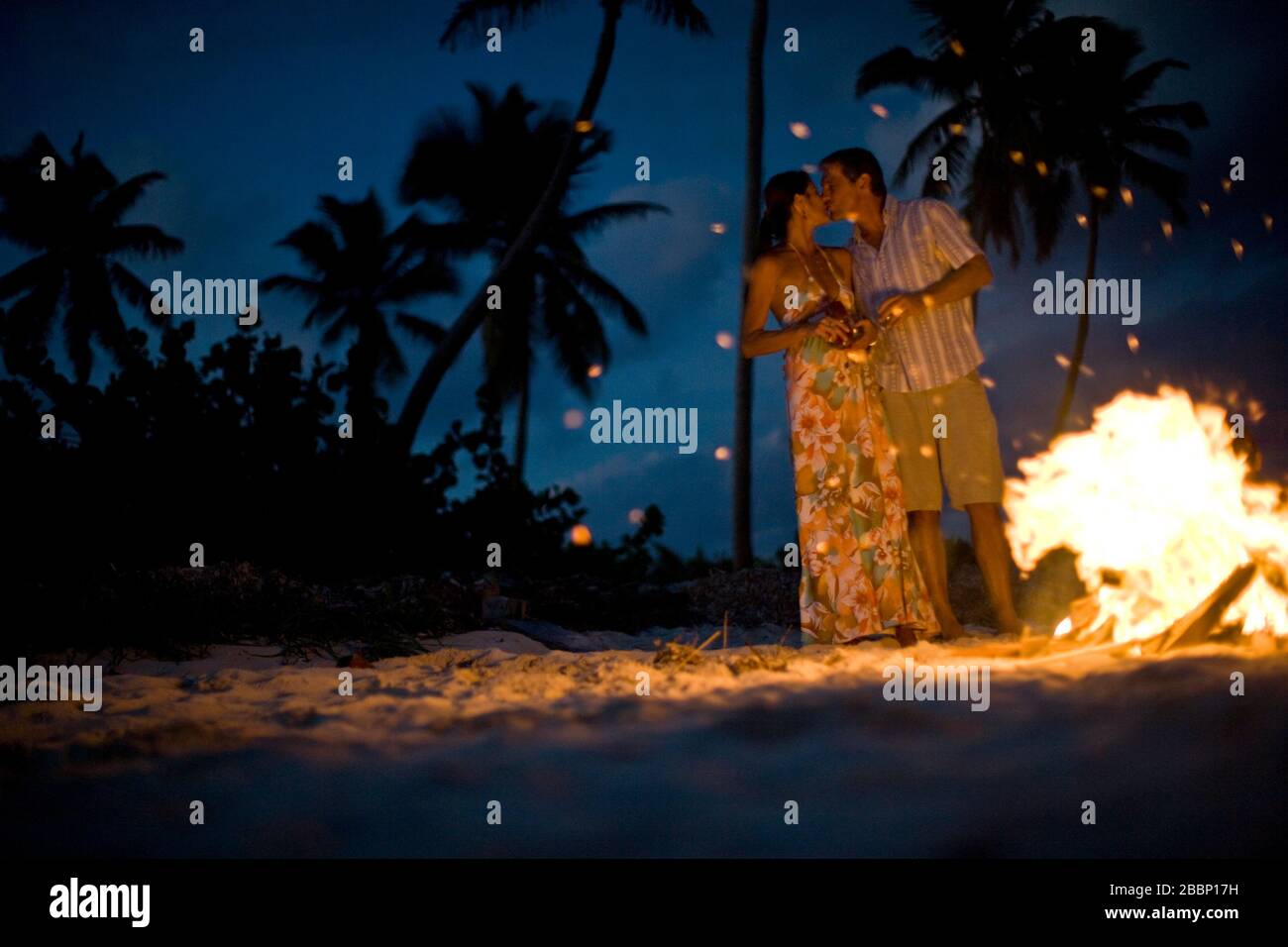Mid-adult couple standing beside a bonfire on a beach Stock Photo - Alamy