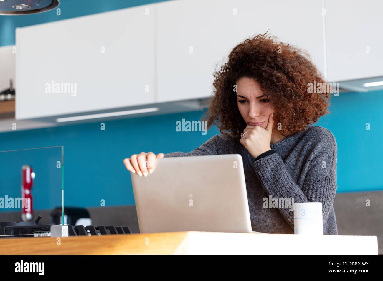 Thoughtful young woman with curly face working at laptop from home ...