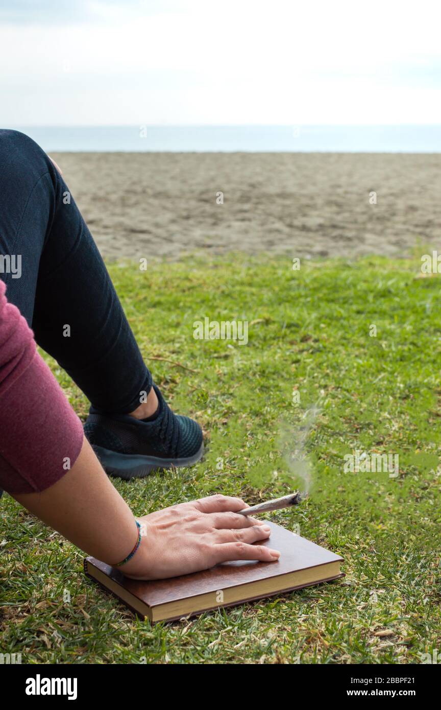 Person reading a book on beach take a break to smoke a marijuana joint ...