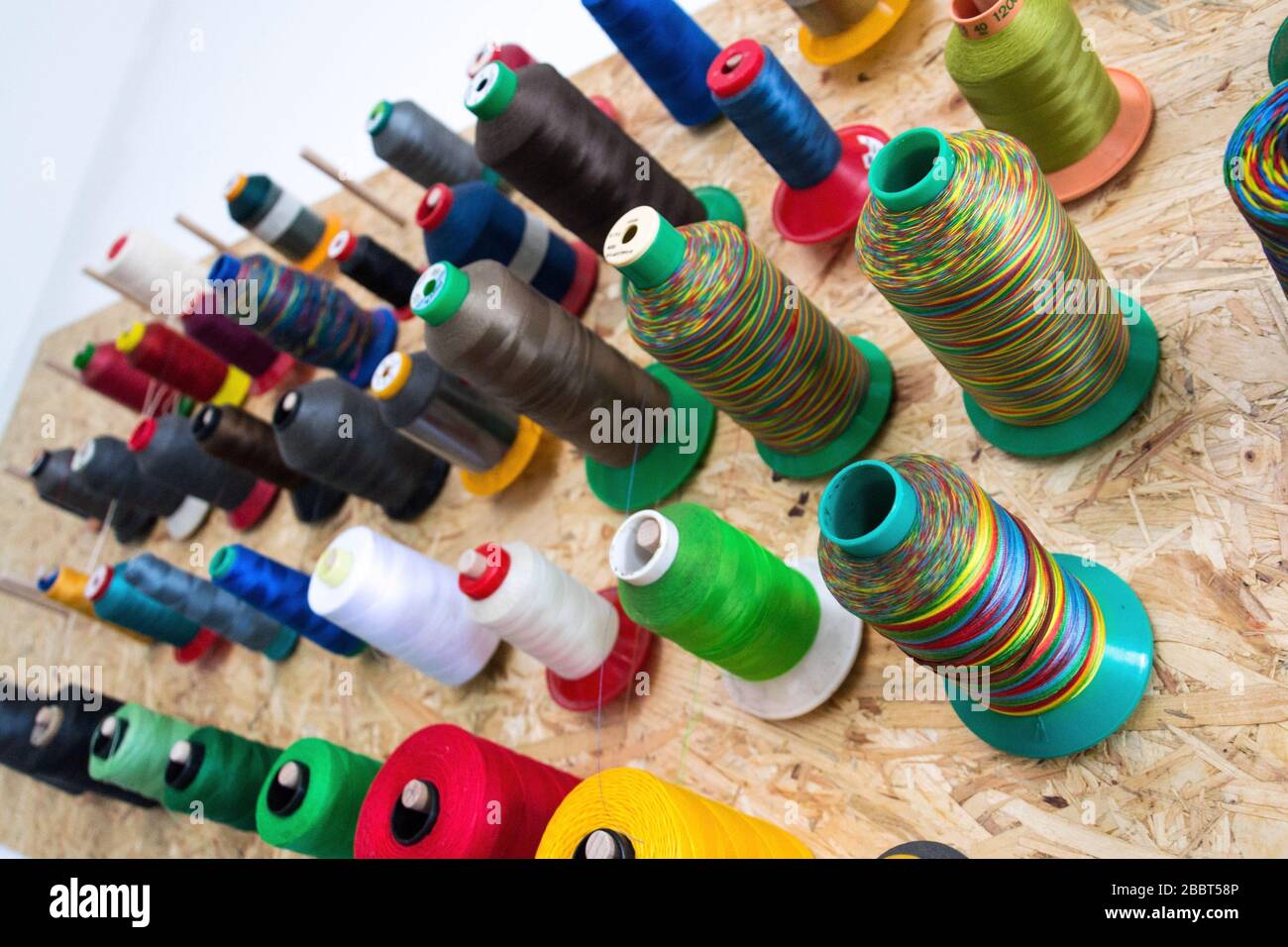 Colorful thread reels on wooden wall set up for sewing machine, textile ...