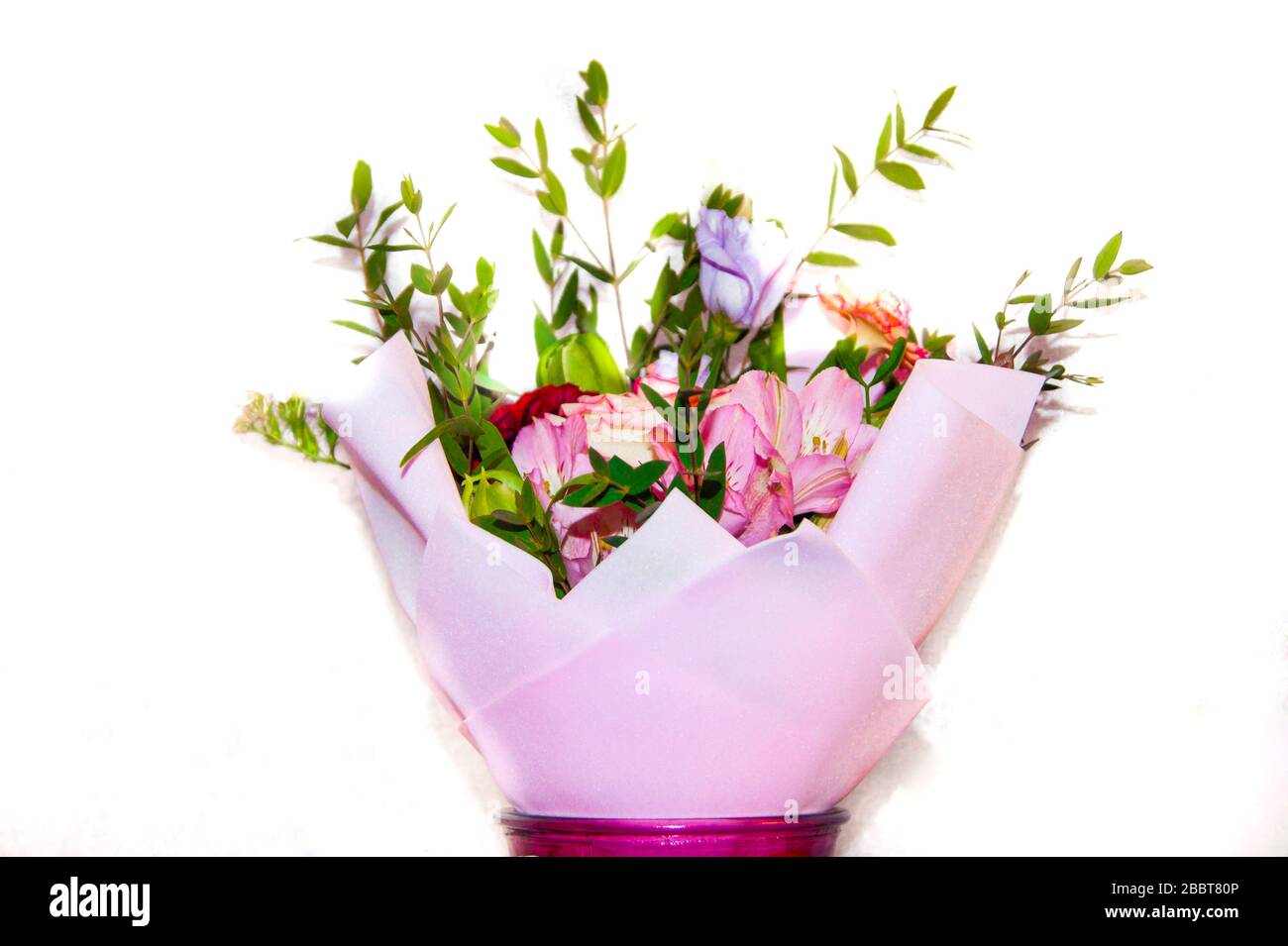 A delicate bouquet of different flowers in a light pink wrapper stands ...
