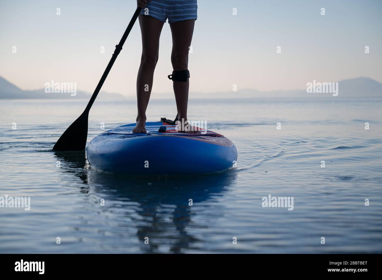 Low angle view of female legs standing on sup board floating on calm ...