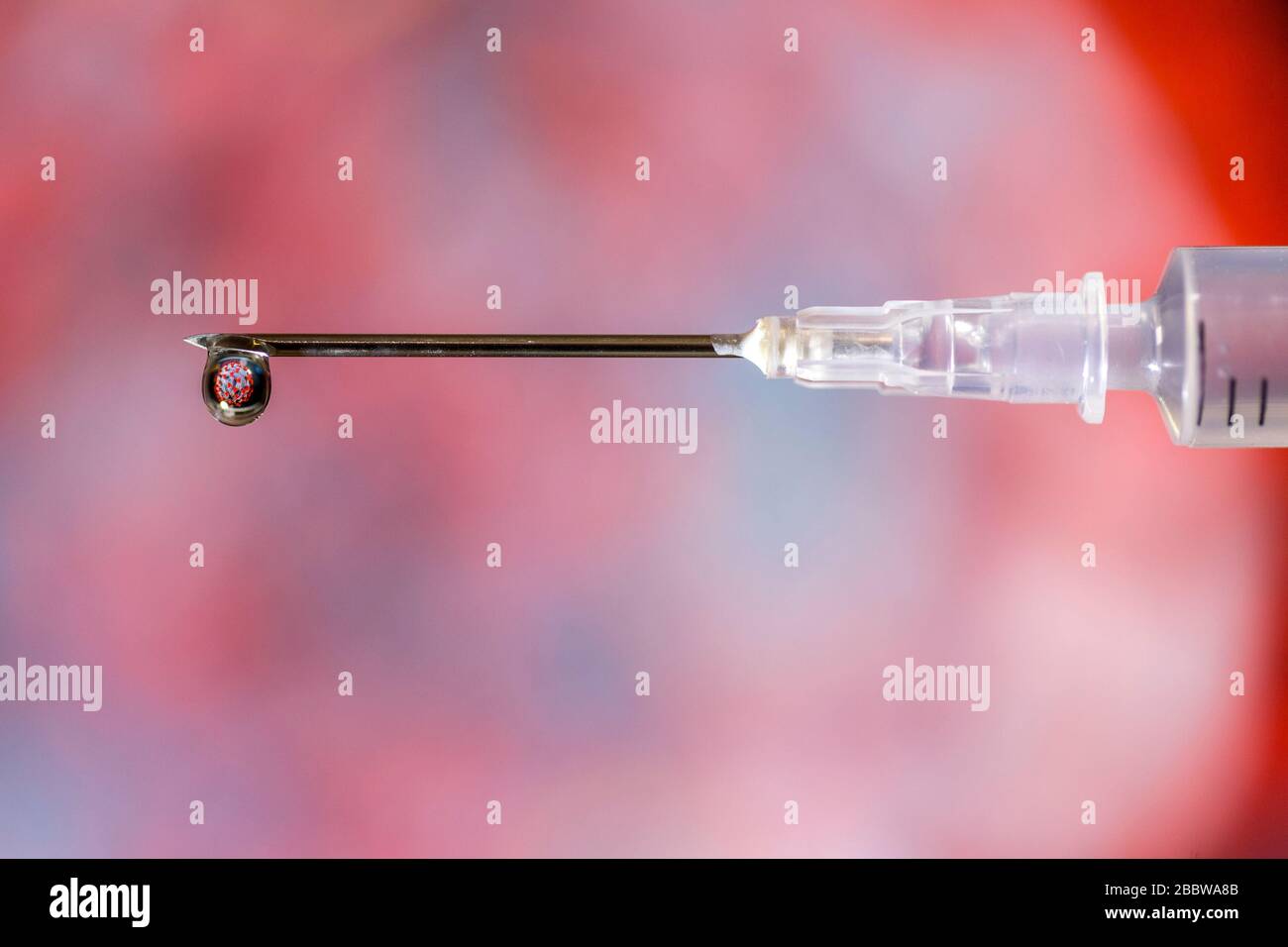 Hypodermic needle dripping fluid over a red and grey out of focus ...