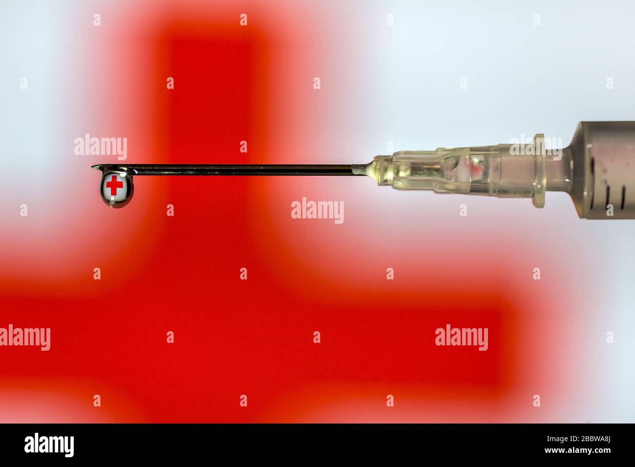 Hypodermic needle dripping fluid with red cross reflected over a red ...