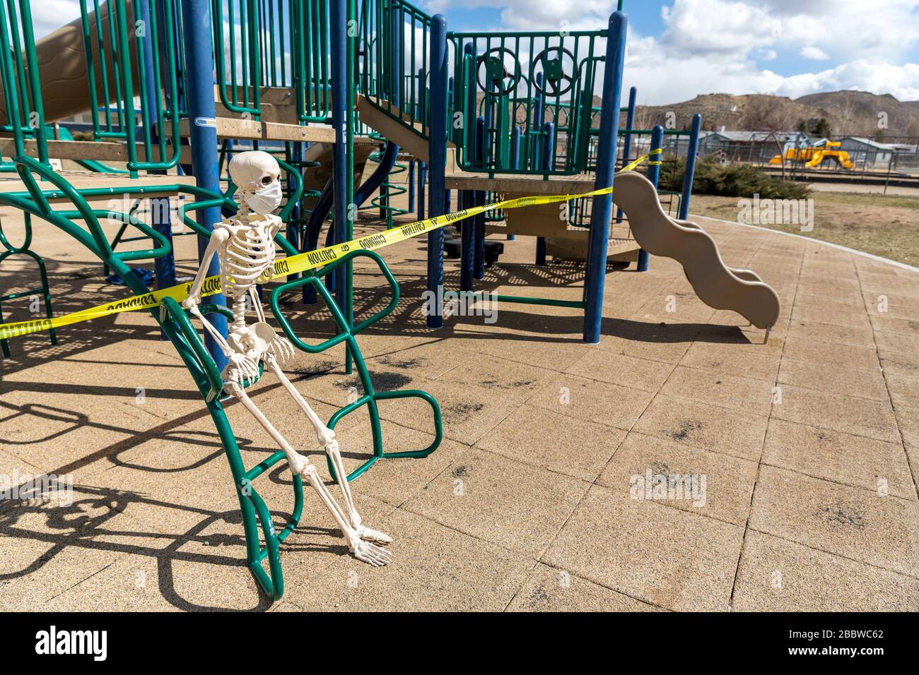 Adult skeleton sitting on playground equipment at an empty closed park ...