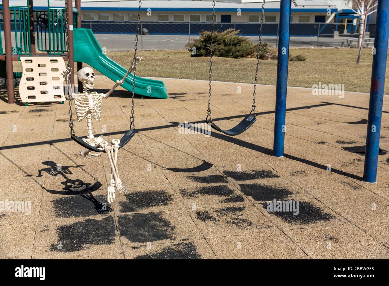 Skeleton swinging on childs toy at an empty closed park on a nice day ...
