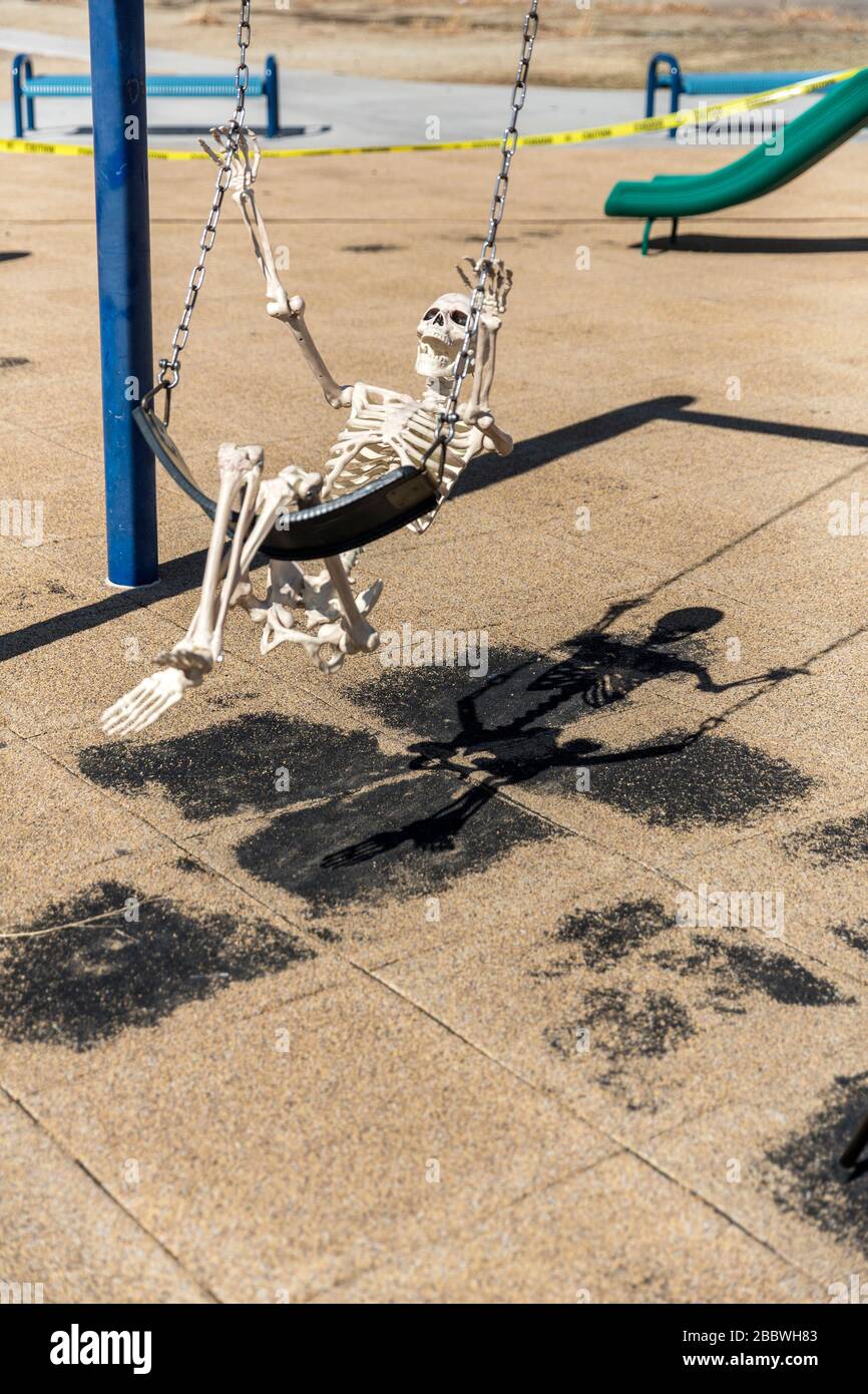 Skeleton swinging on childs toy at an empty closed park on a nice day ...