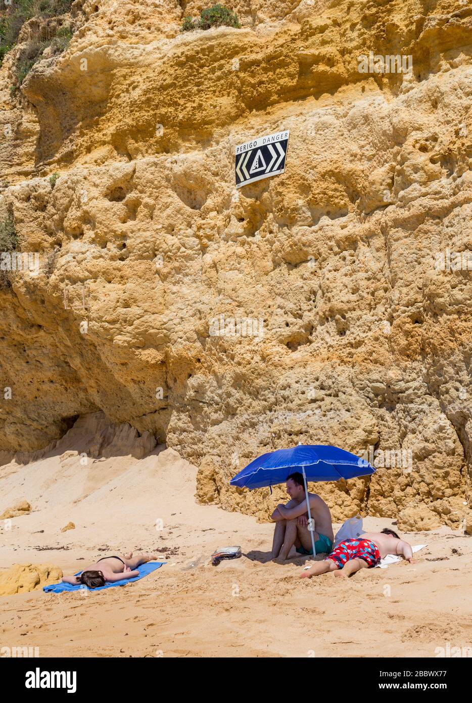 People sunbathing under a danger sign for rockfall, coast west of ...