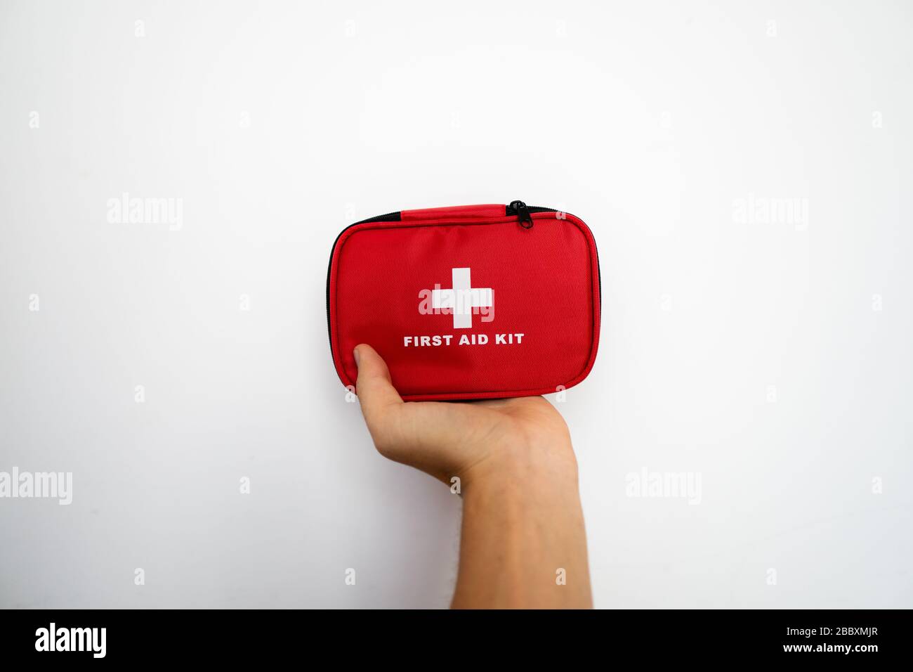 Man's hand holding a red first-aid kit with a white wall on background ...
