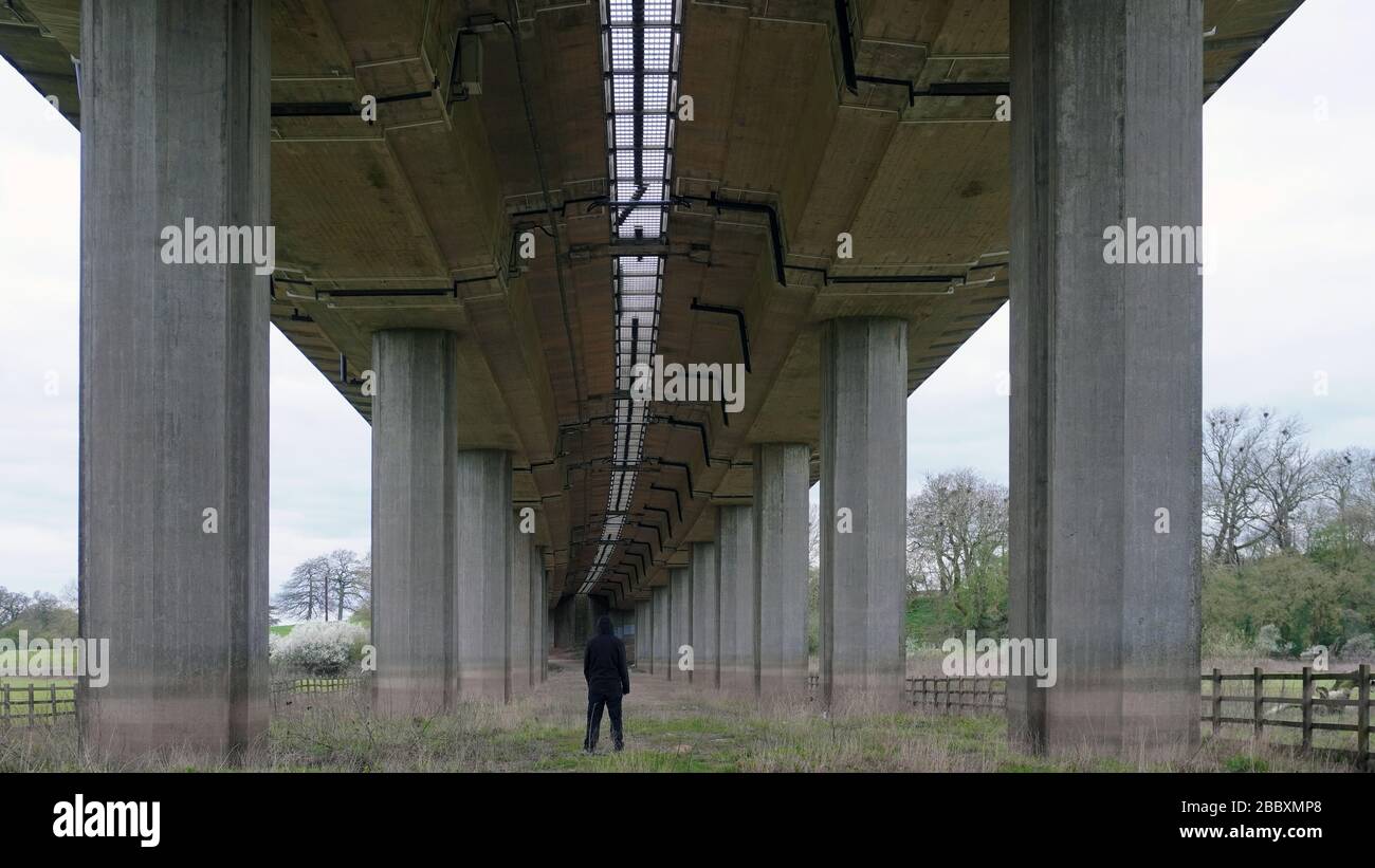 A hooded figure standing underneath a motorway bridge in the ...