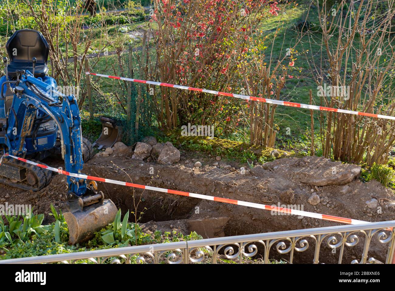 Blue excavator between temporary tape barrier in back yard. Red and ...