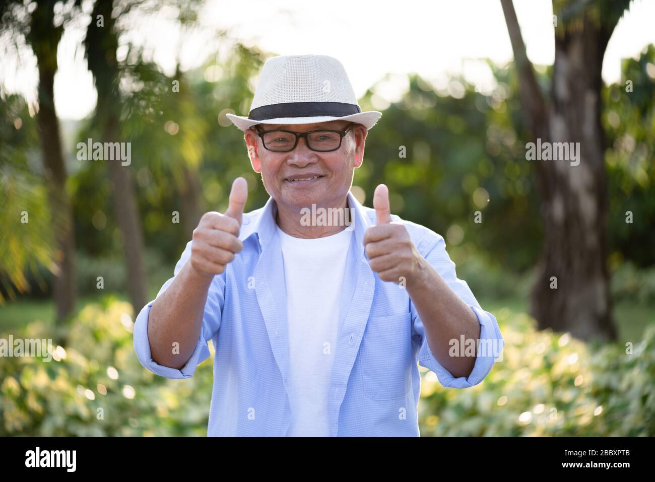 A happy old man with thumbs up smiling and laughing in the garden ...