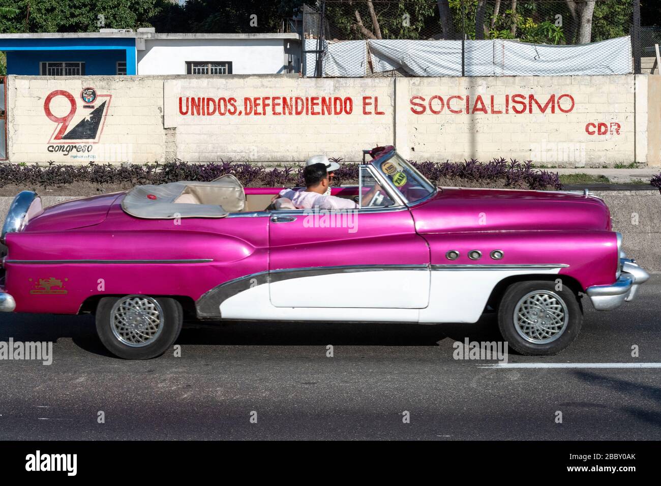 Men driving inside a vintage American car of the 50s past a propaganda ...