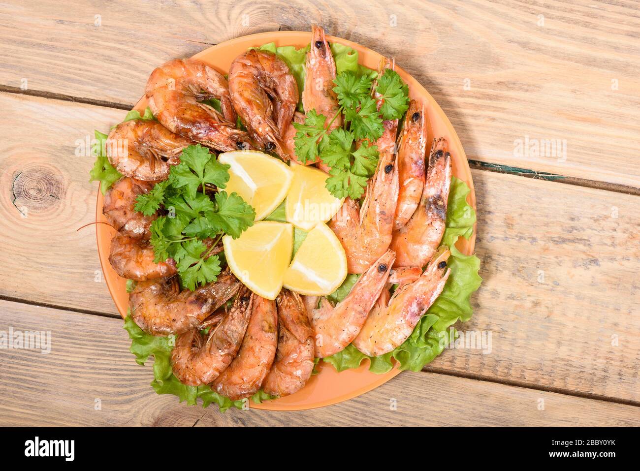 Flat lay. Plate with shrimps, lettuce and parsley on a wooden table ...
